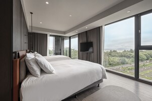 Quarto de hotel moderno com uma cama grande, televisão de tela plana e vista para a cidade.