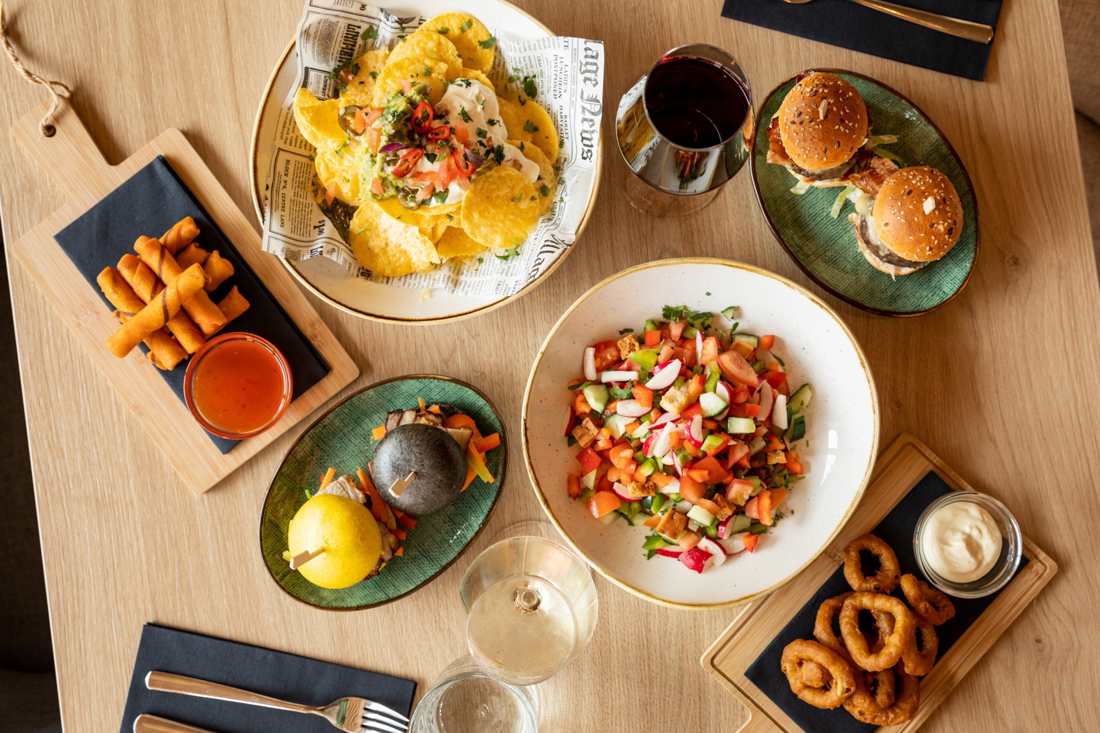 Uma mesa com nachos, hambúrgueres, uma salada e bebidas.