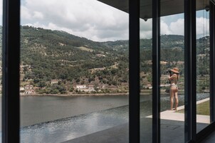 Vista de um edifício moderno com grandes janelas sobre um lago e uma paisagem montanhosa.