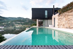 Uma casa moderna com piscina, muro de pedra e vista para a paisagem ao redor.