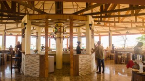 Um espaço amplo e interno, com estrutura central de madeira, vários espaços para sentar e vista para o exterior.