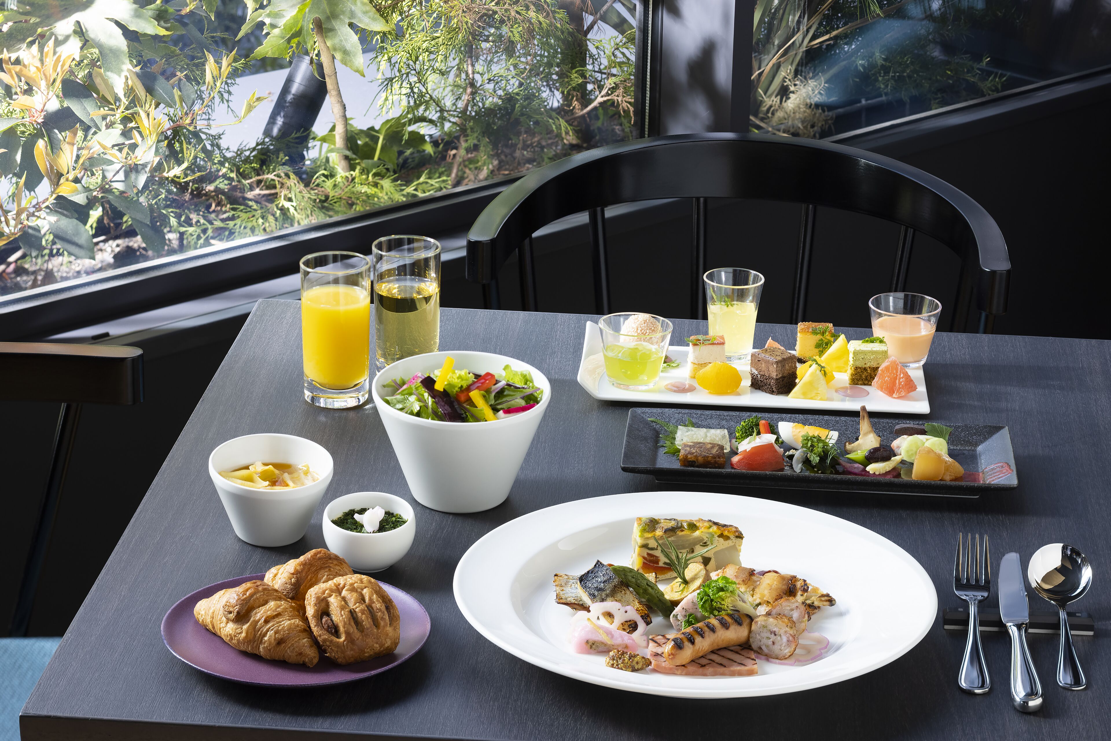 Uma mesa de jantar com itens de café da manhã, incluindo croissants, uma salada e diversas bebidas.