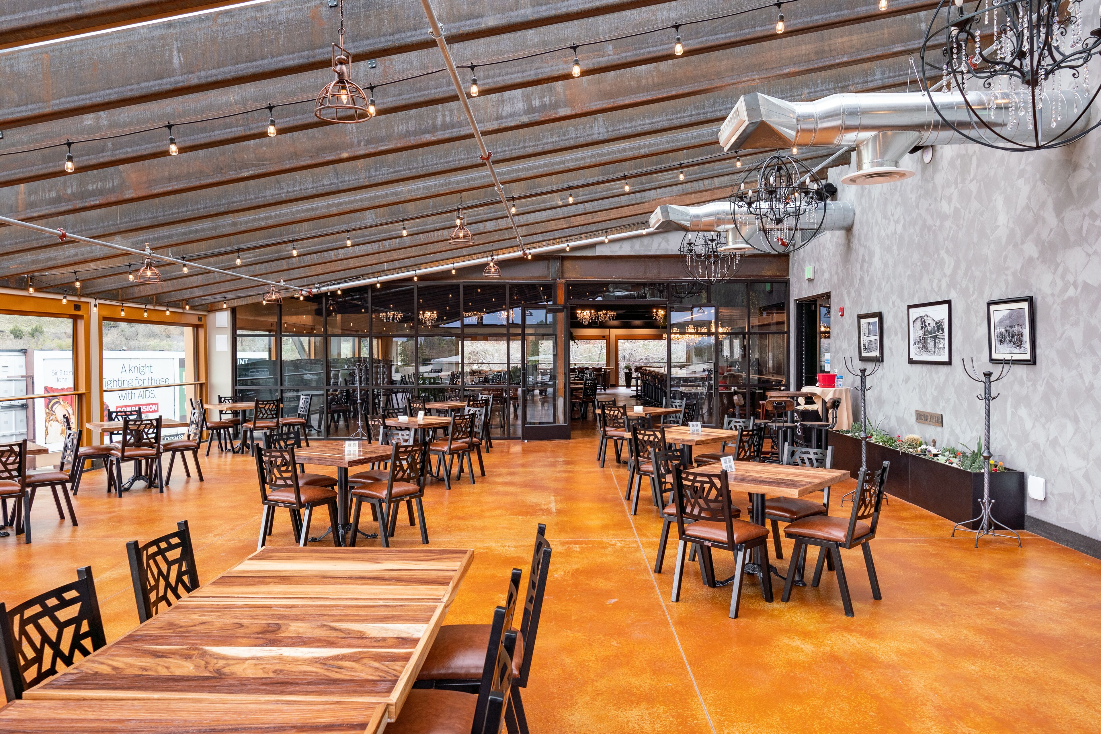 Um restaurante espaçoso com pé direito alto, dutos aparentes e diversos arranjos de mesas e cadeiras.
