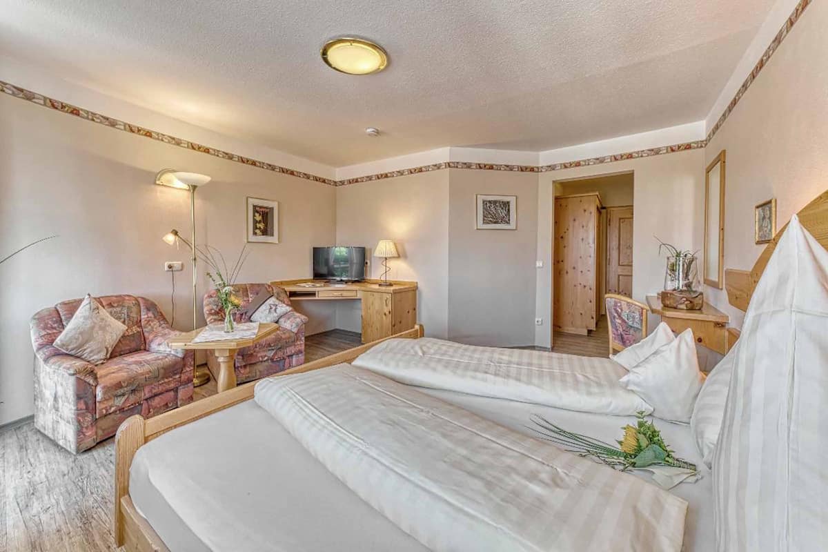 Quarto de hotel com cama, escrivaninha, cadeira e televisão.