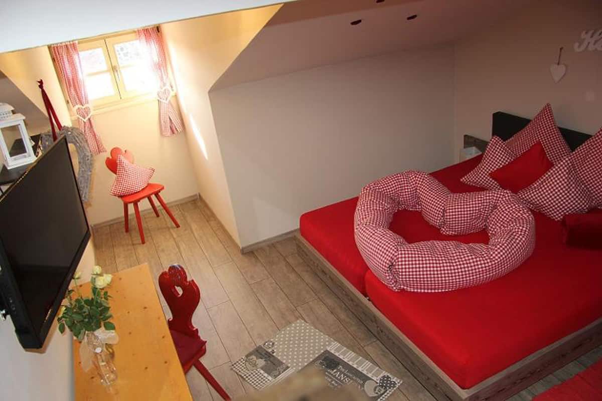 Espaço compacto com um sofá vermelho, uma pequena mesa de jantar com cadeiras e uma TV sobre um suporte.