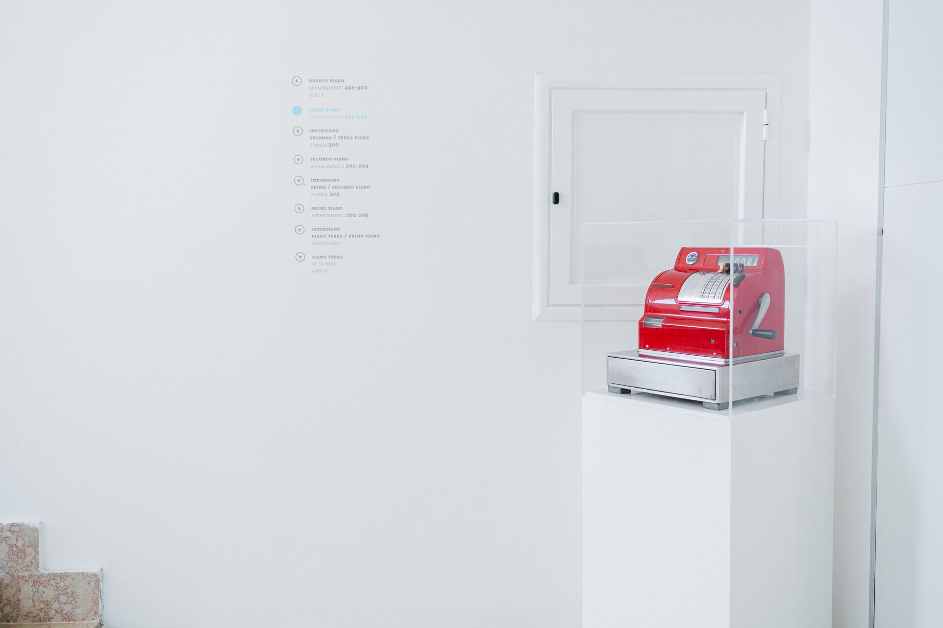 Máquina automática vermelha numa sala branca, com uma lista de tipos de quartos e números na parede.
