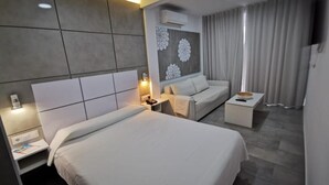 Quarto de hotel moderno com uma cama grande, um sofá, uma mesinha e uma televisão.