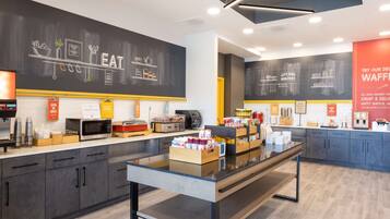 Um café moderno com cardápio em lousa, estação de café por autoatendimento e um balcão com diversas opções de comida.