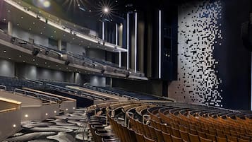 Um teatro moderno com assentos em níveis, um carpete estampado e uma grande tela digital exibindo um design pixelizado.