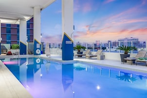 Piscina interior moderna com sinalização clara das regras, espreguiçadeiras e vista para a cidade.