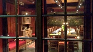 Uma sala de jantar com uma mesa comprida posta para várias pessoas, rodeada de cadeiras.