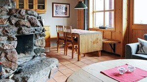 Interior rústico de cabana com lareira de pedra, mesa de jantar de madeira e um espaço de estar acolhedor.
