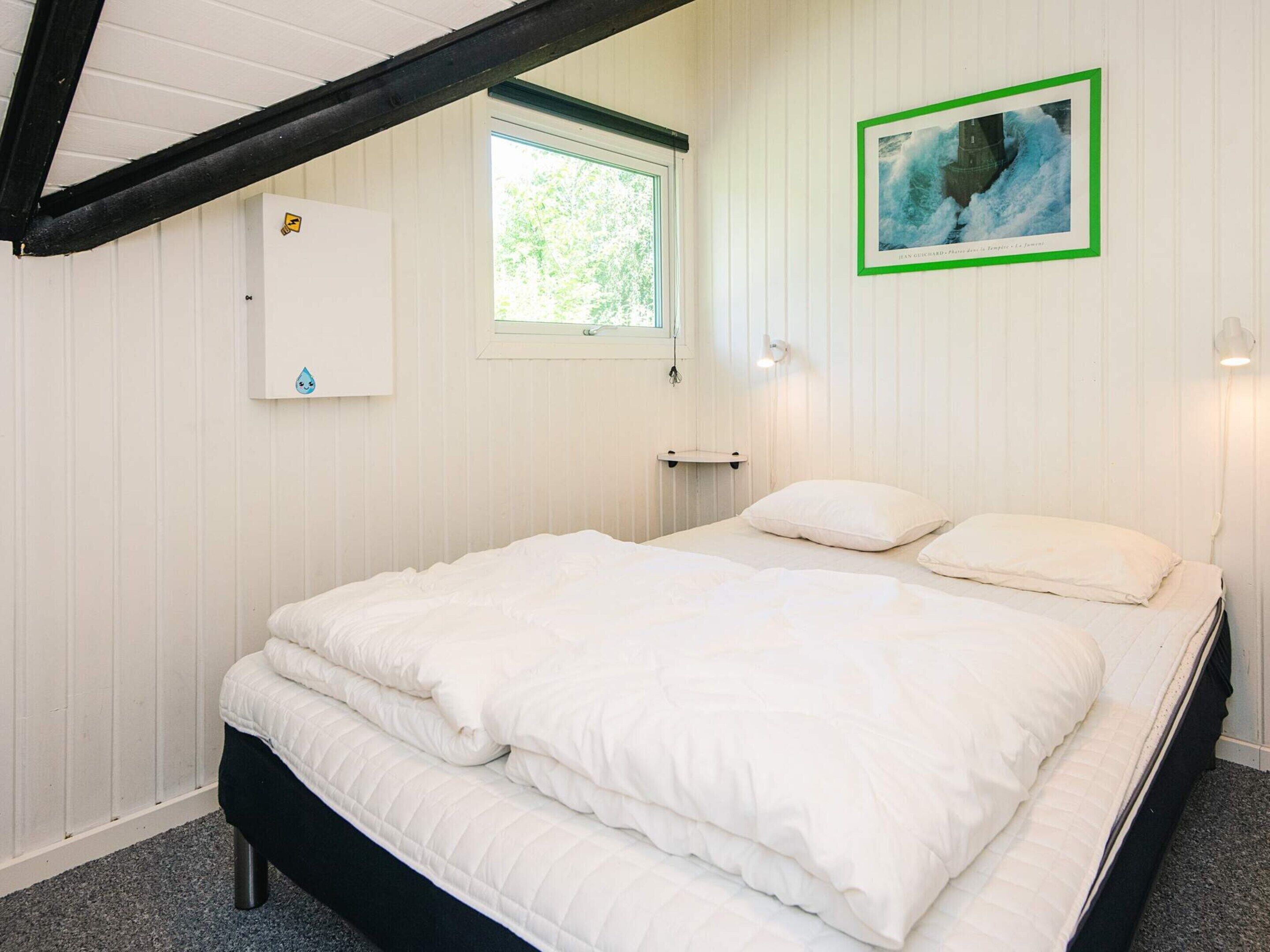 Quarto com cama, janela, luminária na parede e quadro emoldurado.