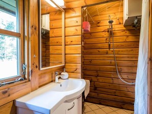 Casa de banho de cabana de madeira, com lavatório, espelho e chuveiro.