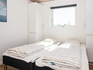Uma cama de solteiro com colcha branca e padrão floral, cabeceira preta e janela com vista para o exterior.