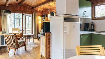 Interior de uma cabana de madeira com área de jantar, cozinha e uma janela.
