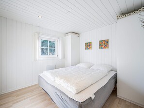 Quarto com cama, janela e duas pinturas coloridas na parede.