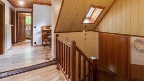 Interior de madeira com teto inclinado, escada e um pequeno claraboia.