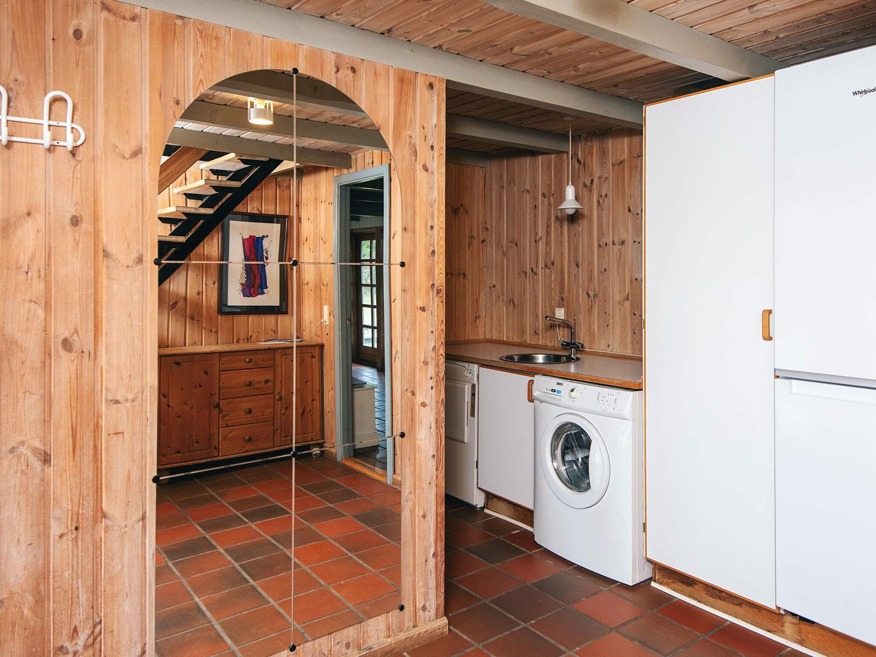 Cozinha compacta com máquina de lavar, armários de madeira e piso ladrilhado.