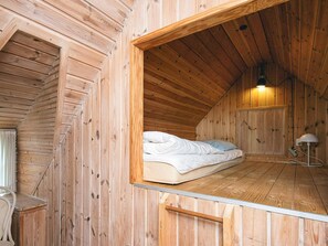 Quarto de cabana de madeira com beliche, escrivaninha e luminária.
