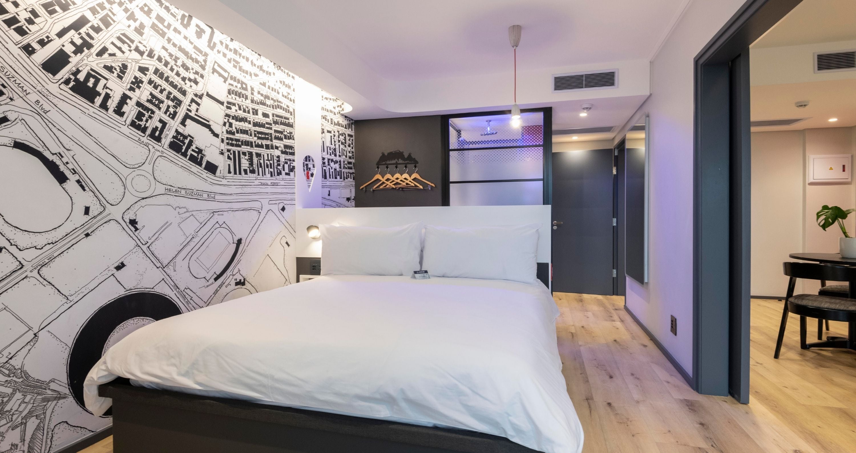 Quarto de hotel moderno com uma cama grande, um mapa na parede, uma mesinha com uma cadeira e um cabideiro.