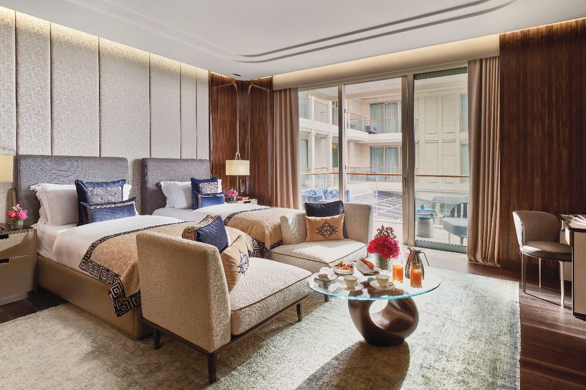 Quarto de hotel com duas camas, um sofá, uma mesa de centro de vidro e vista para a varanda.