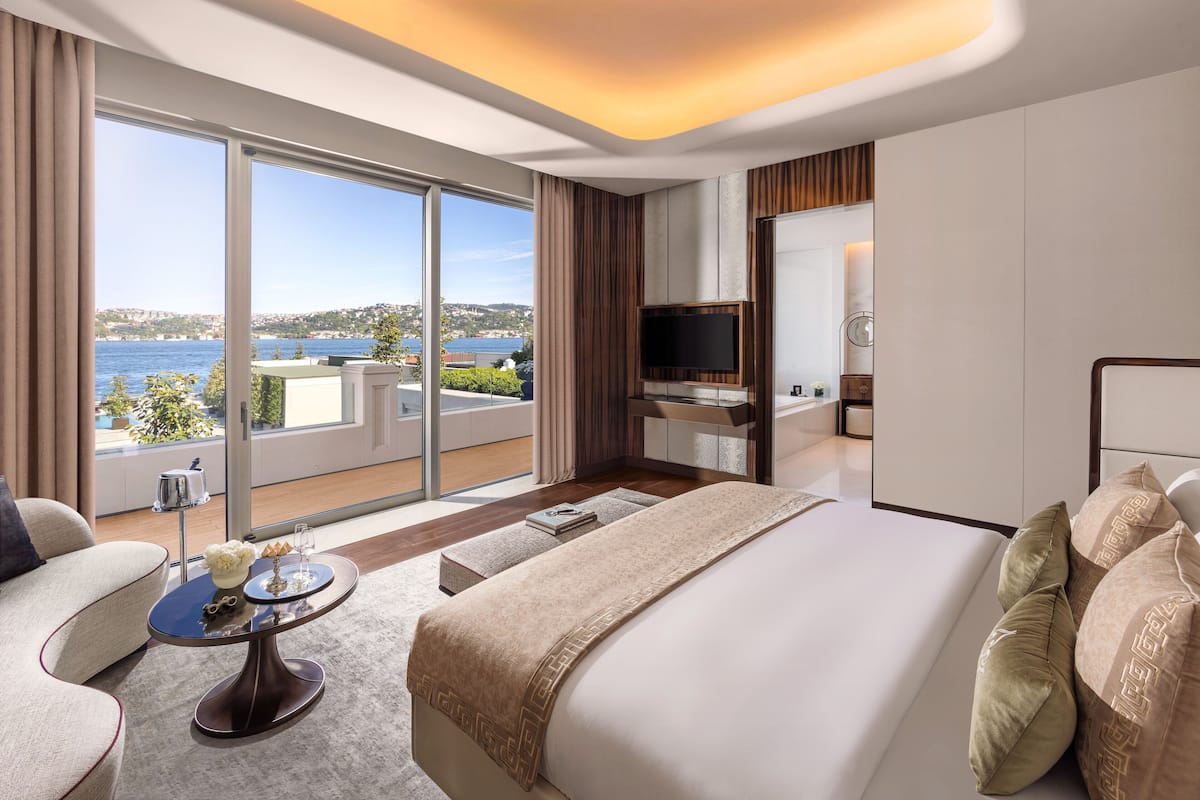 Quarto de hotel moderno com uma cama grande, televisão e varanda com vista para o mar.