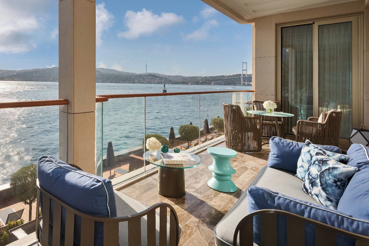 Uma varanda com vista para o mar e uma ponte, mobiliada com um sofá, cadeiras e uma mesa.