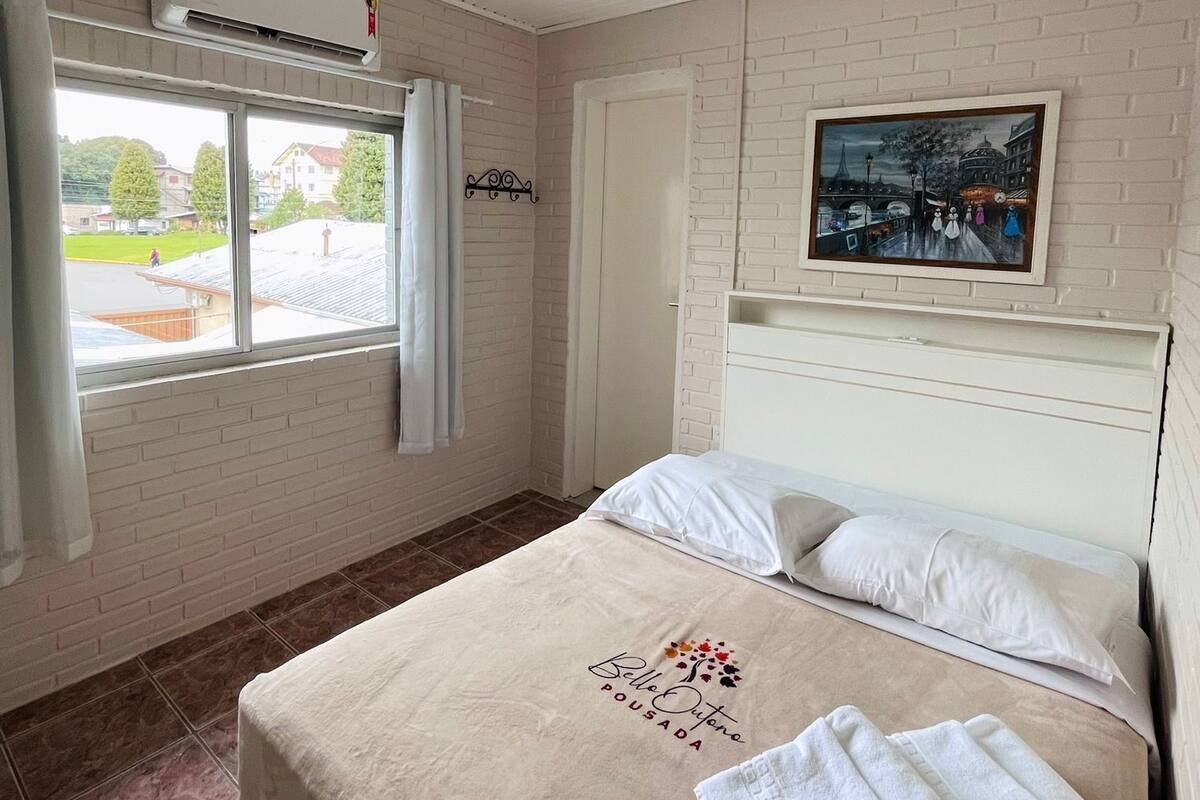Quarto de hotel com cama, janela com cortinas, quadro na parede e ar condicionado.