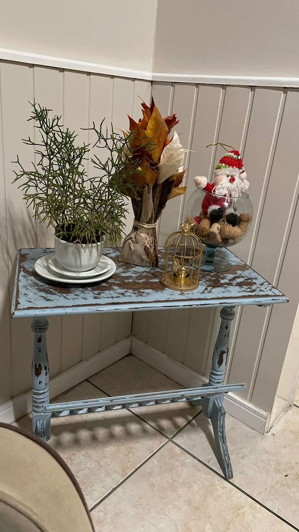 Uma mesa pequena e rústica com uma planta, folhas secas, uma gaiola de pássaro e uma figura de Natal.