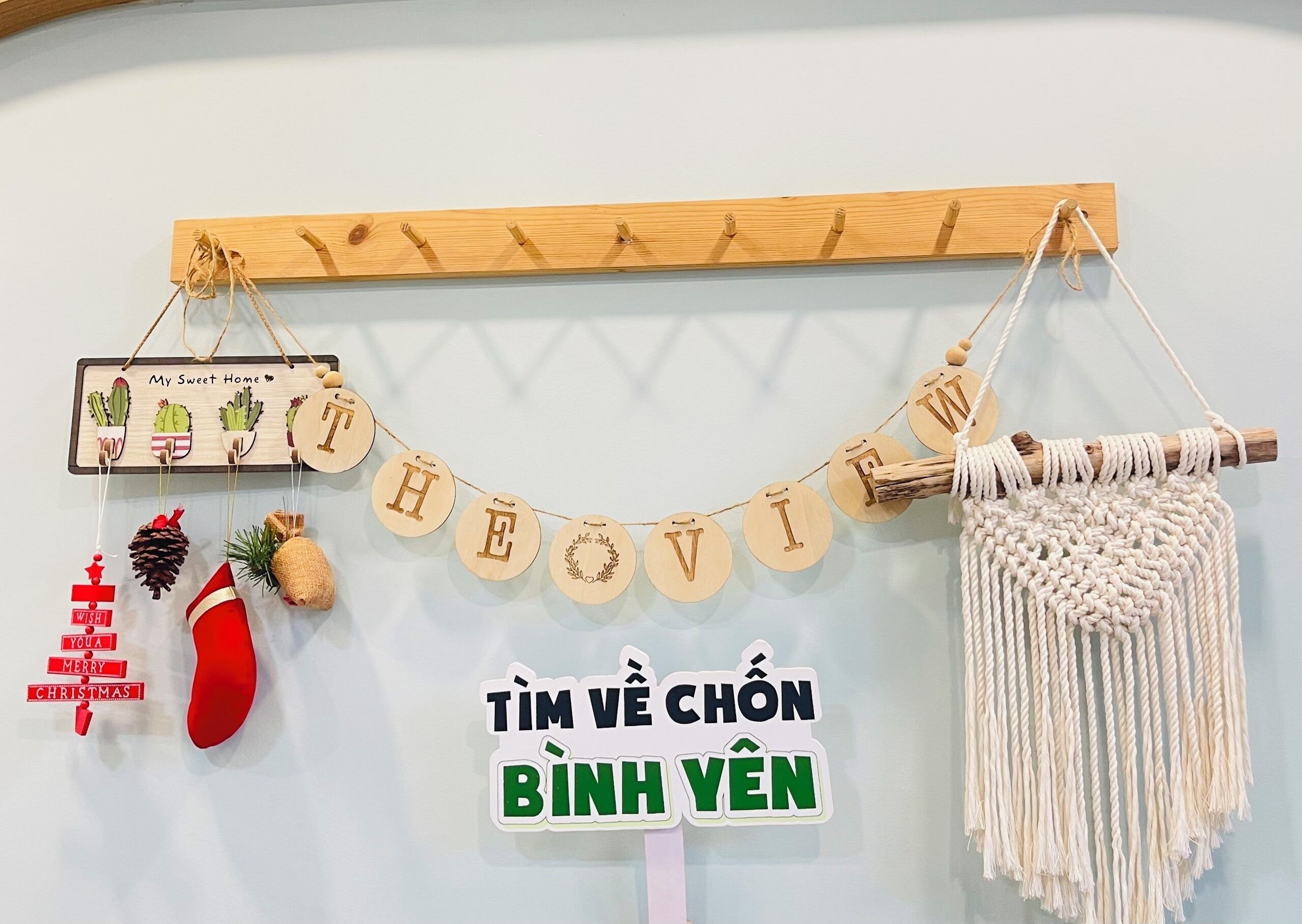 Pareda com um letreiro de madeira, uma peça de macramé e um banner com letras.