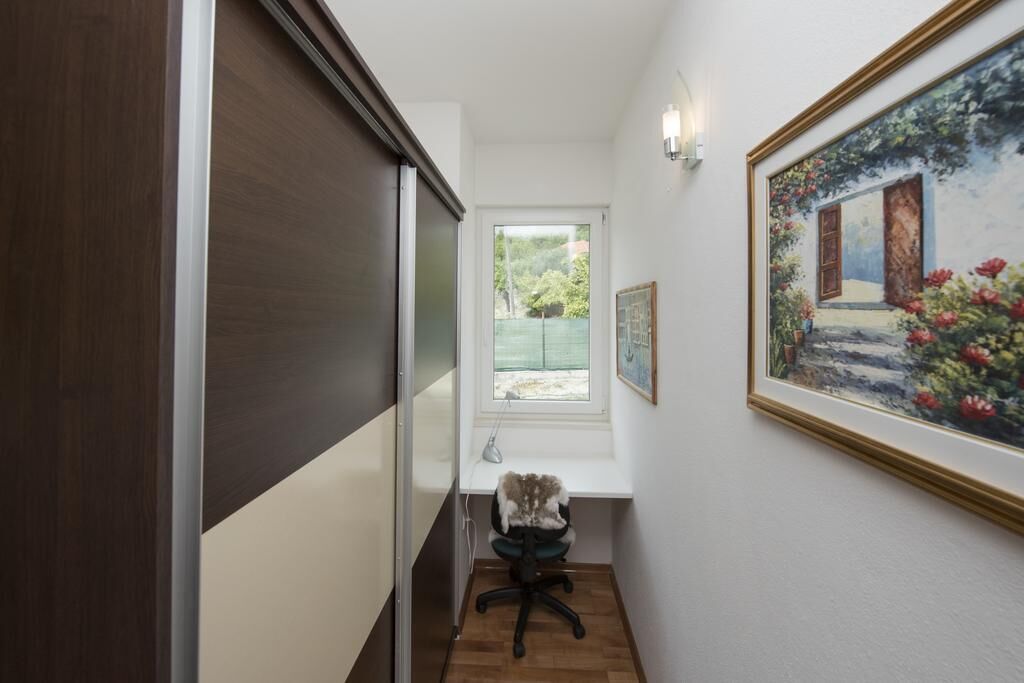 Um corredor estreito com uma mesa e uma cadeira, uma janela com vista para o verde e um quadro pendurado na parede.