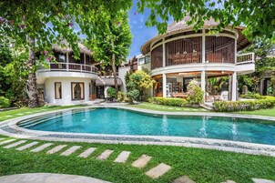 Uma villa luxuosa com piscina, estrutura de colmo e vegetação exuberante.