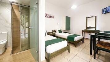 Quarto de hotel com chuveiro, duas camas, escrivaninha, cadeira, espelho e televisão.