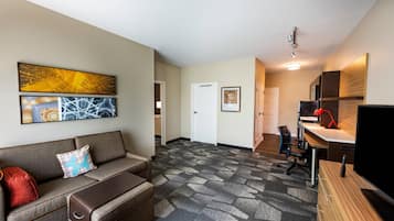 Quarto de hotel com sofá, escrivaninha, televisão e obras de arte nas paredes.