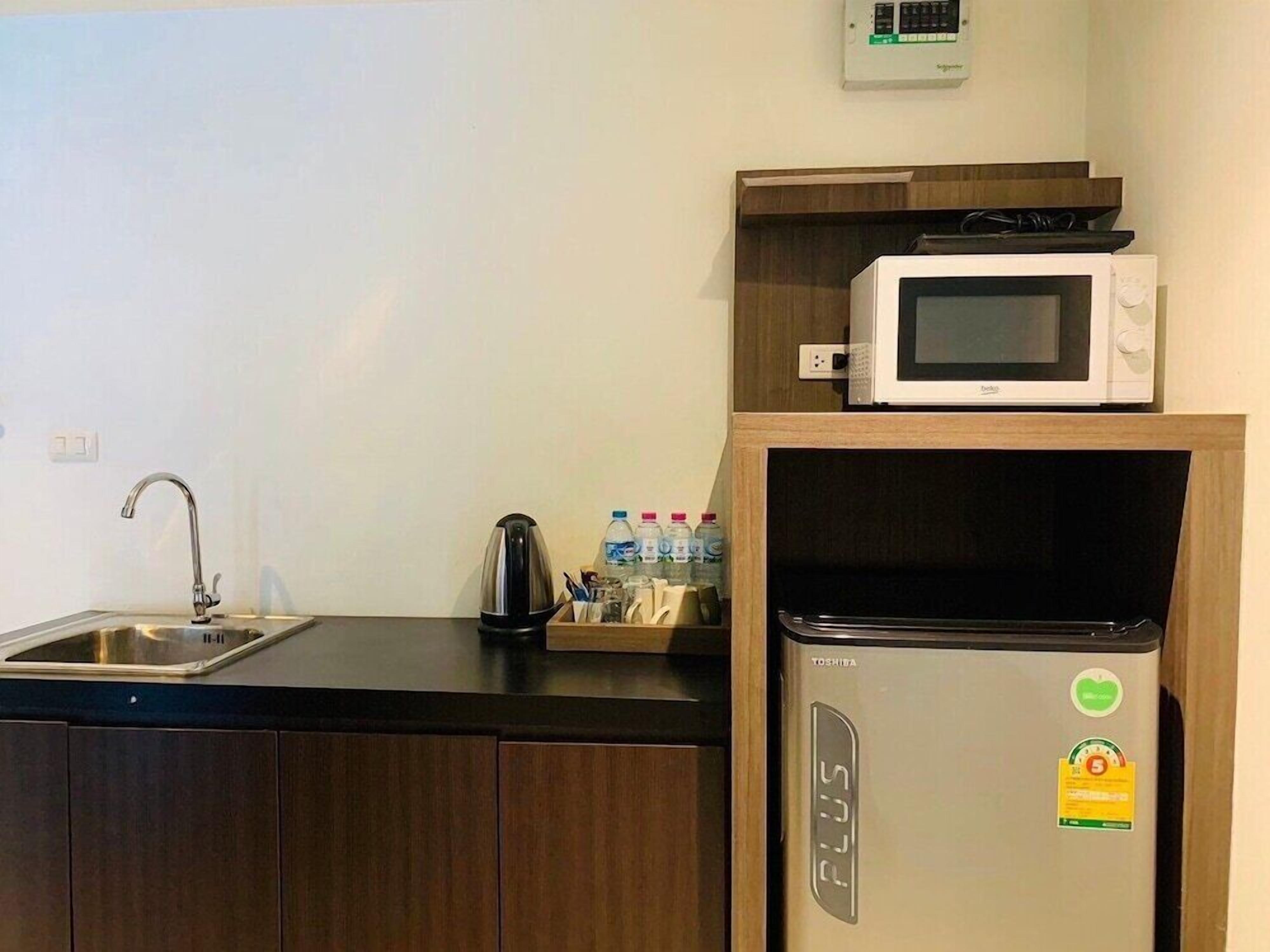 Uma cozinha compacta com pia, chaleira, micro-ondas e geladeira.