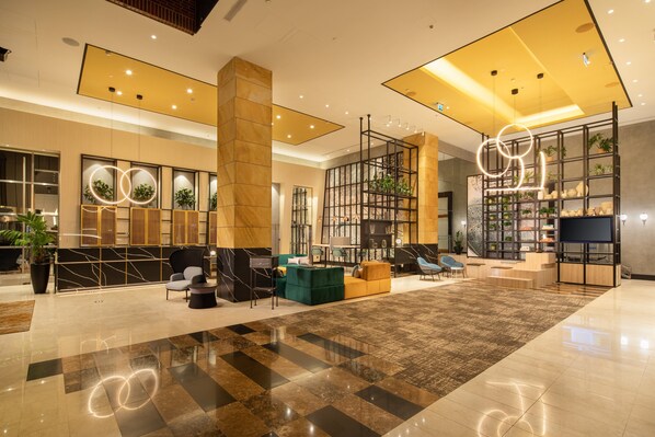 Um hall amplo com balcão de check-in, áreas de estar, mesa de recepção e um grande arranjo de plantas.