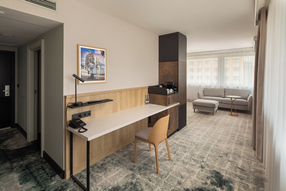 Quarto de hotel moderno com uma escrivaninha de madeira, uma cadeira, um sofá e uma máquina de café.