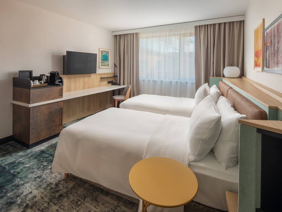Quarto de hotel com duas camas, uma escrivaninha, televisão e uma mesinha.