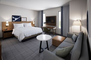 Quarto de hotel moderno com cama, escrivaninha, televisão, sofá e uma pequena mesa.