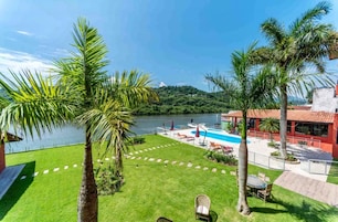 Área de piscina com vista para um lago, cercada por palmeiras e um edifício vermelho.