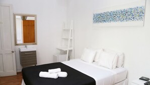 Quarto com cama, mesa de cabeceira, guarda-roupa, espelho e uma obra de arte na parede.