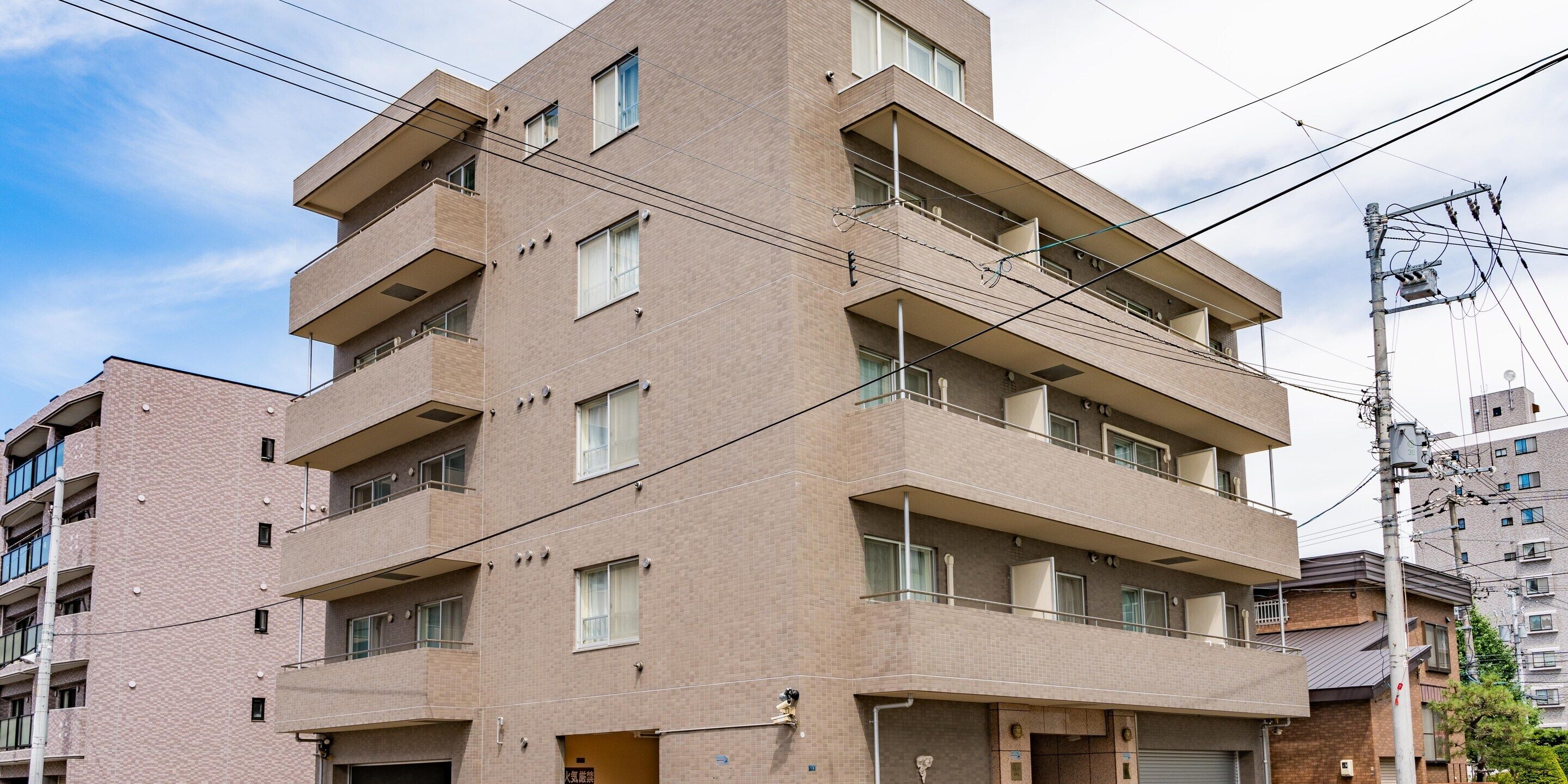 Um edifício residencial com vários andares, varandas, uma porta de garagem e linhas de serviços visíveis.