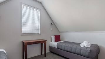 Quarto pequeno e bem arrumado, com uma cama de solteiro, mesa de cabeceira e janela com persianas.
