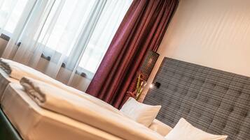 Quarto de hotel moderno com uma cama grande, cabeceira e janela com cortinas translúcidas.