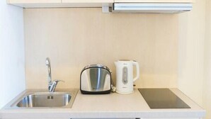 Uma cozinha compacta com uma pia de aço inoxidável, uma torradeira e uma chaleira sobre o balcão.