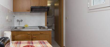 Uma cozinha compacta com armários de madeira, uma pia de aço inoxidável e uma mesa com toalha xadrez.