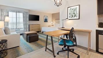 Quarto de hotel com cama, escrivaninha, cadeira, televisão e cozinha.