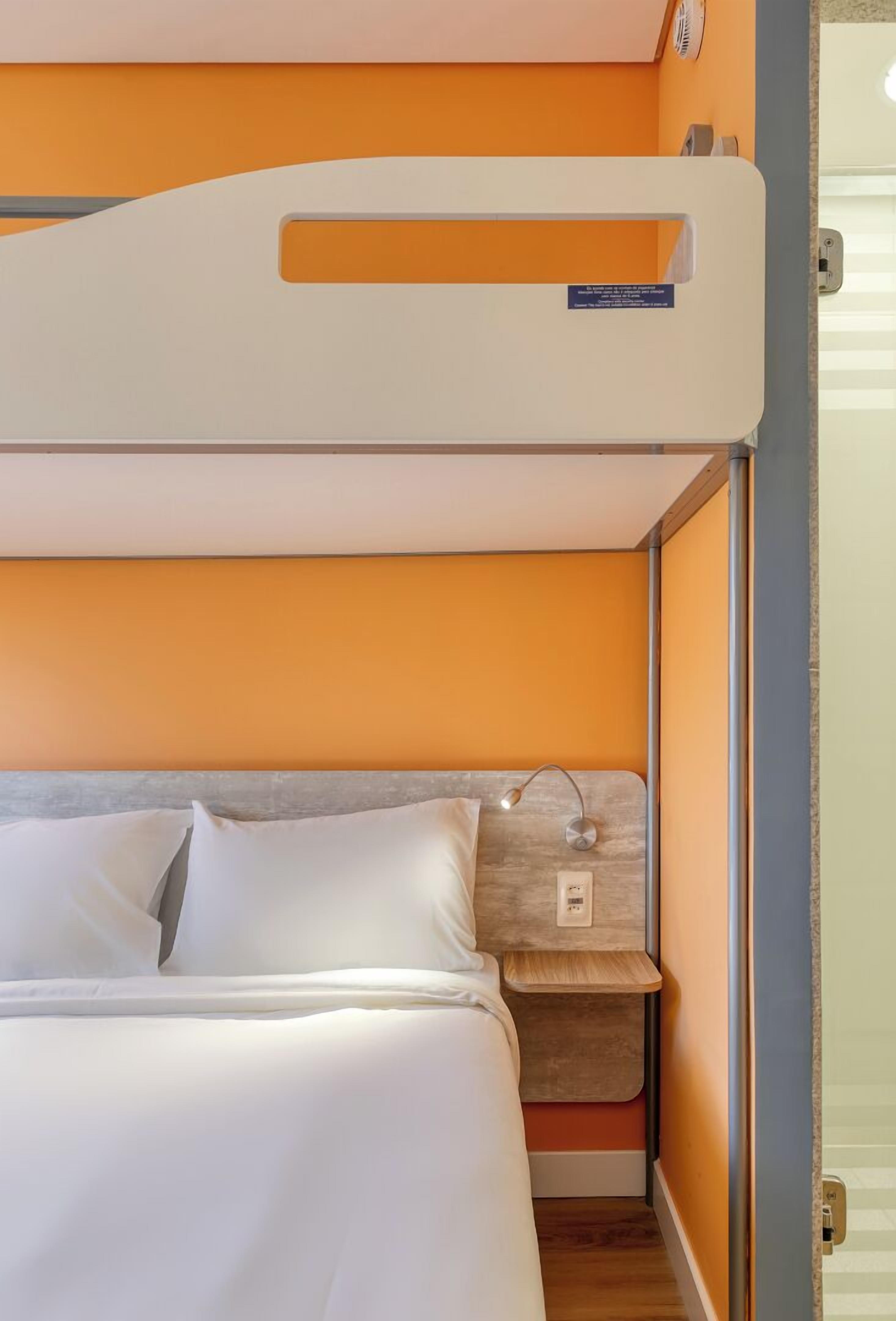 Uma cama beliche com cabeceira, mesa de cabeceira e luminária fixada na parede.
