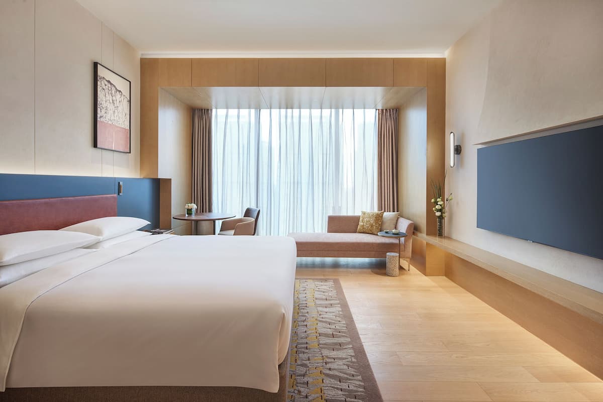 Quarto de hotel moderno com uma cama grande, um sofá, uma mesa pequena e uma televisão.